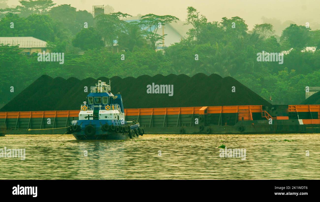 Morning traffic at Mahakam River, Samarinda. Tugboat towing huge barge ...