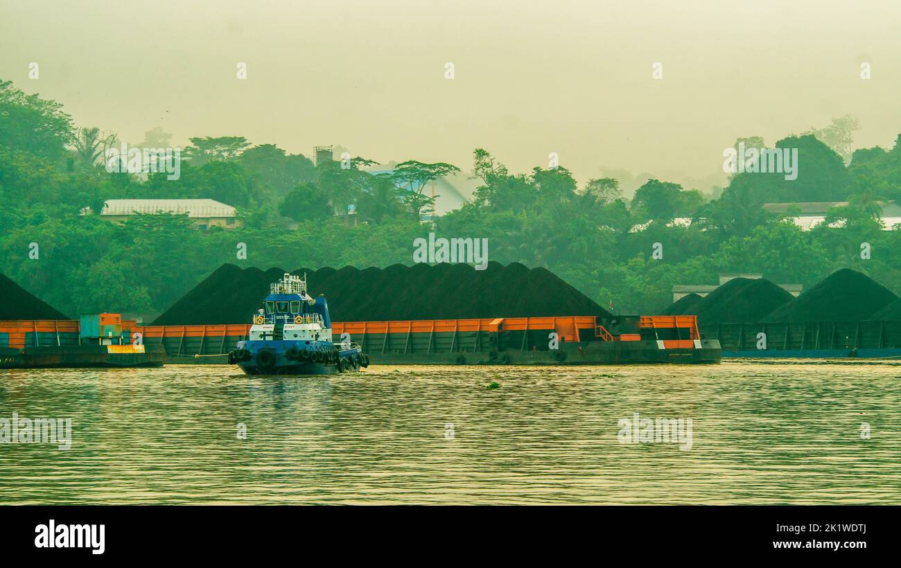 Morning traffic at Mahakam River, Samarinda. Tugboat towing huge barge ...