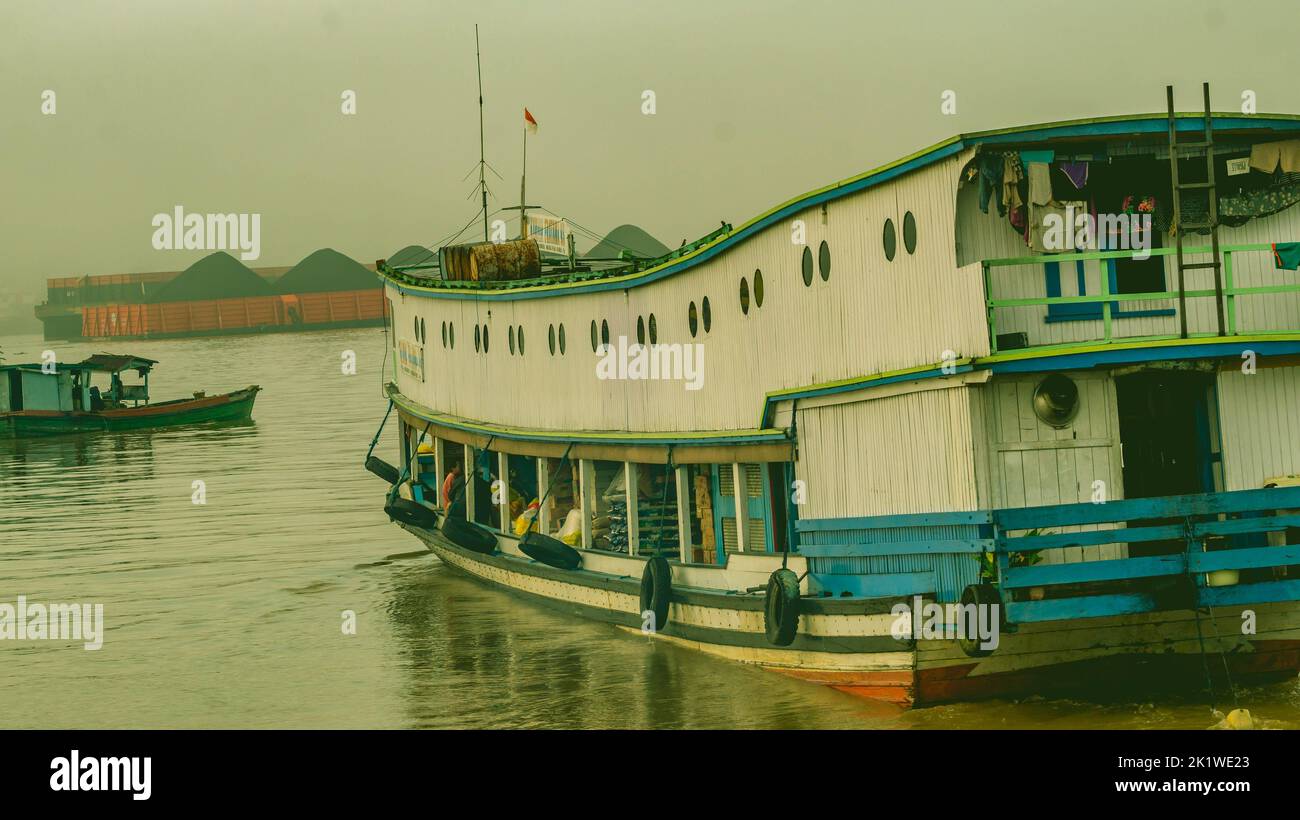 Long wooden boat loaded by passengers and goods cruising Mahakam River ...