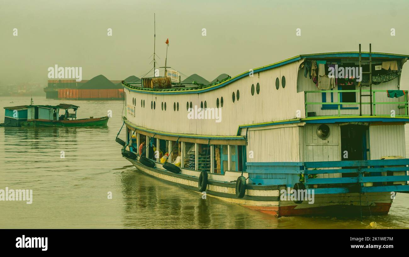 Long wooden boat loaded by passengers and goods cruising Mahakam River ...