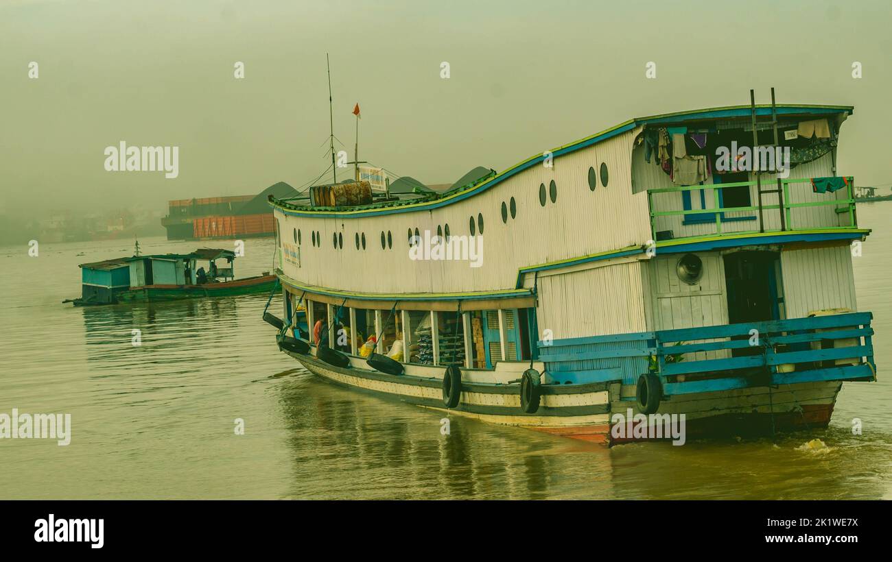 Long wooden boat loaded by passengers and goods cruising Mahakam River ...