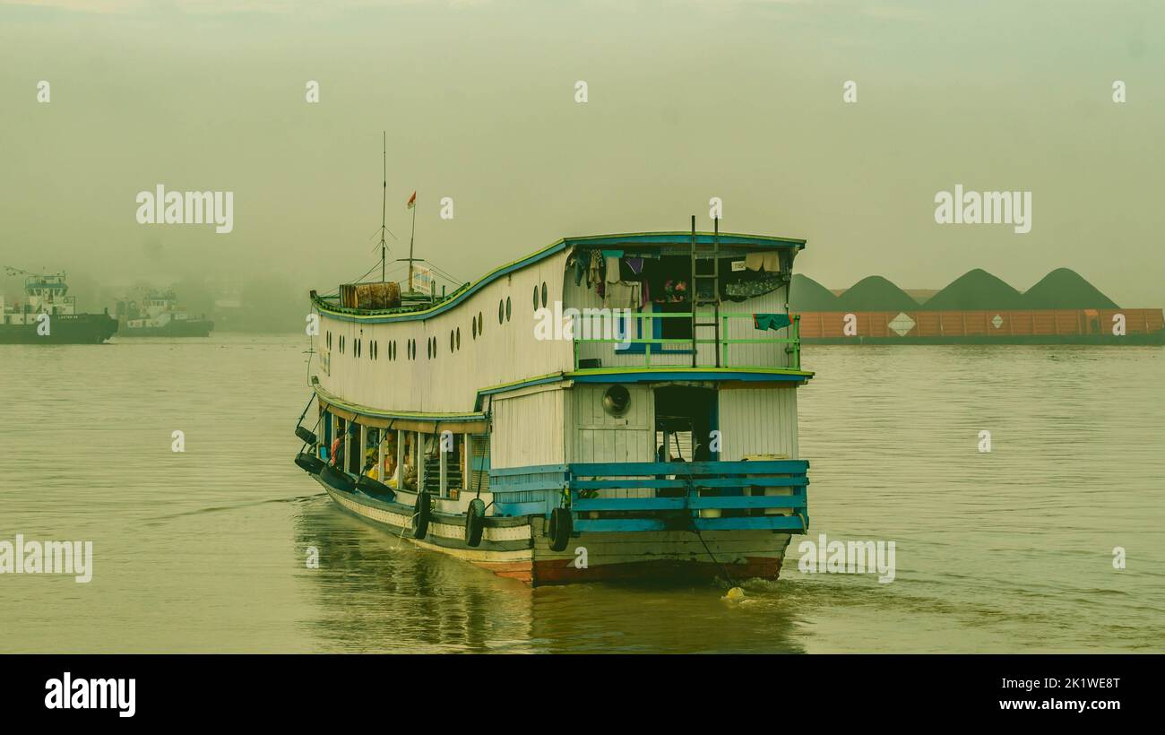 Long wooden boat loaded by passengers and goods cruising Mahakam River ...