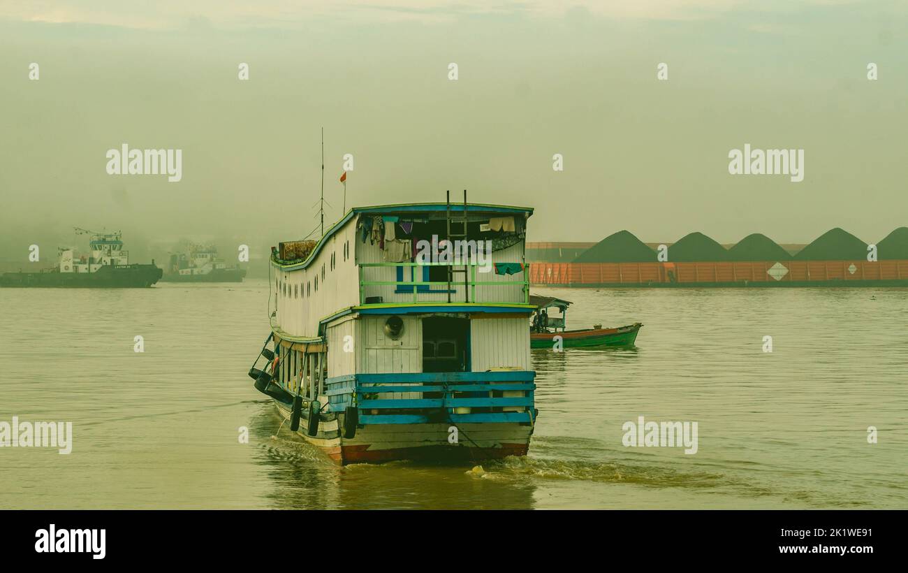 Long wooden boat loaded by passengers and goods cruising Mahakam River ...