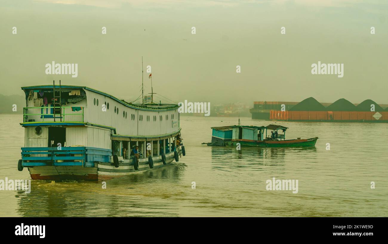 Long wooden boat loaded by passengers and goods cruising Mahakam River ...