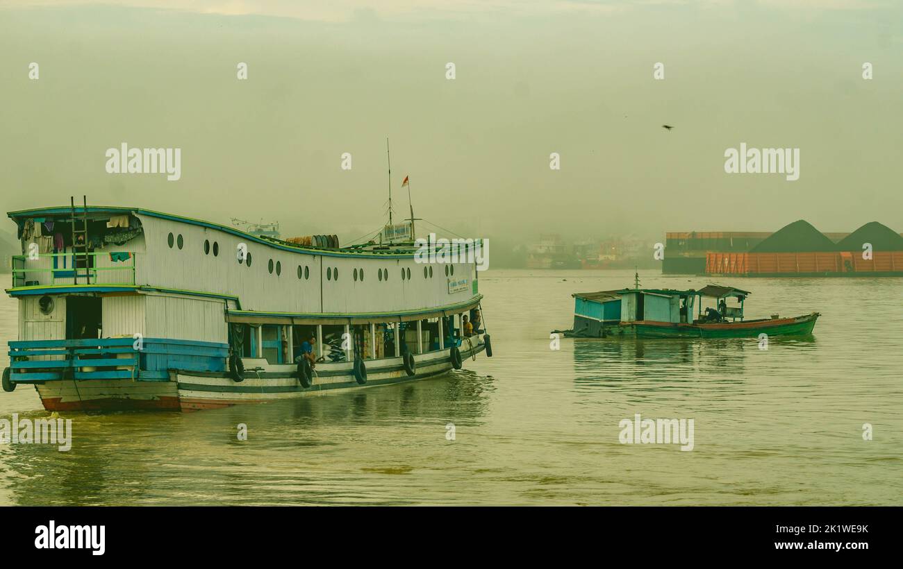 Long wooden boat loaded by passengers and goods cruising Mahakam River ...