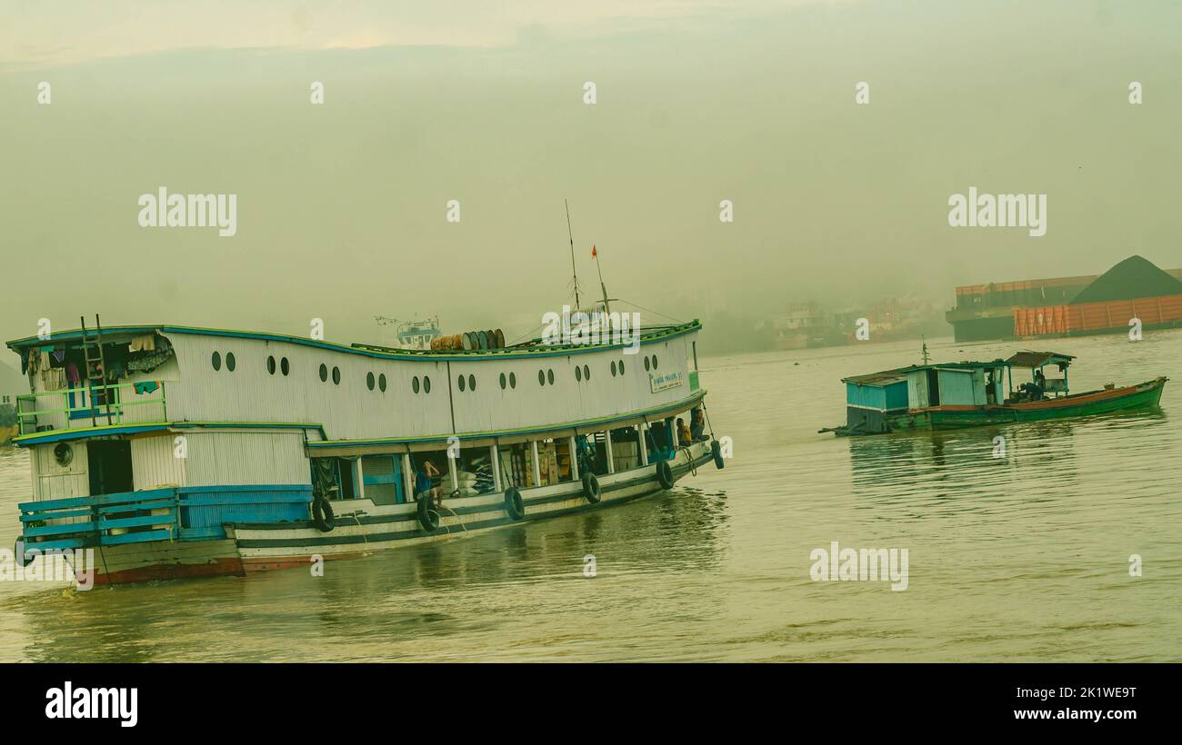 Long wooden boat loaded by passengers and goods cruising Mahakam River ...