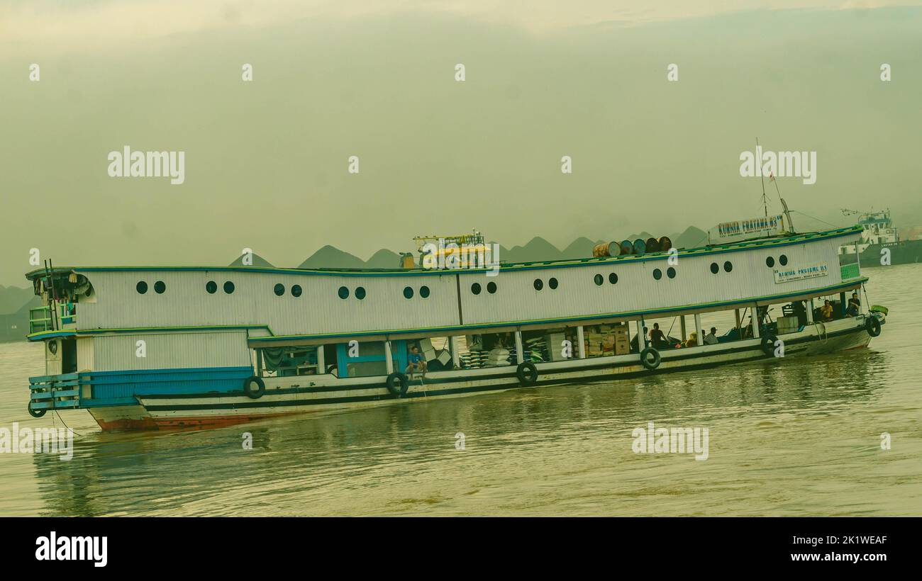 Long wooden boat loaded by passengers and goods cruising Mahakam River ...
