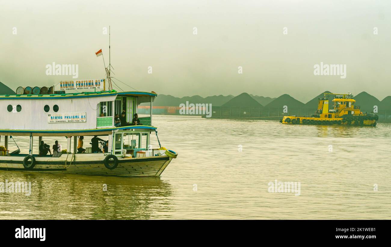 Morning traffic at Mahakam River, Samarinda. Tugboat towing huge barge ...