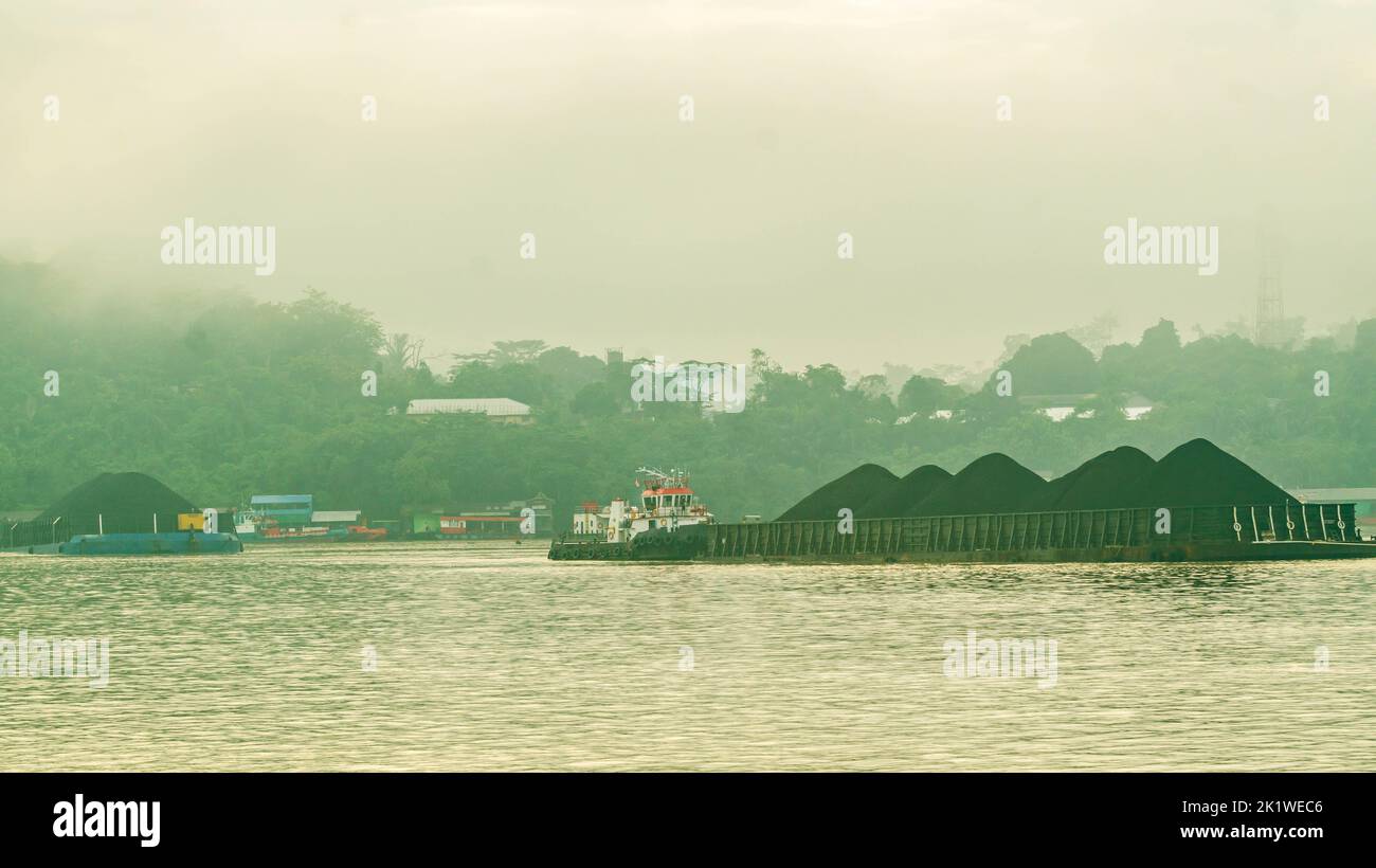 Morning traffic at Mahakam River, Samarinda. Tugboat towing huge barge ...