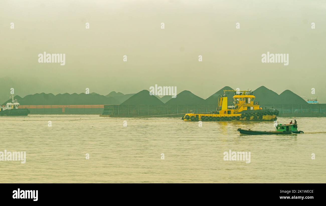 Morning traffic at Mahakam River, Samarinda. Tugboat towing huge barge ...
