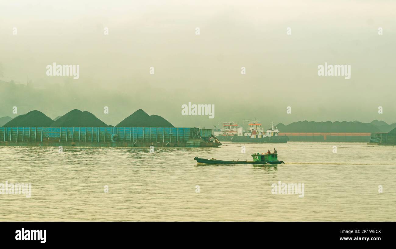 Morning traffic at Mahakam River, Samarinda. Tugboat towing huge barge ...