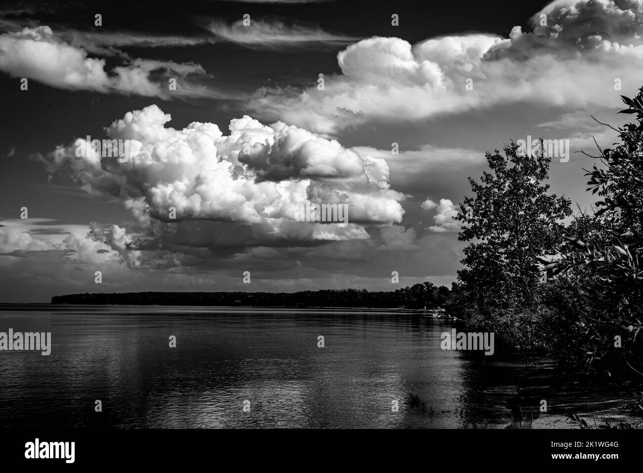 Dramatic black and white image of large white clouds over a calm lake ...