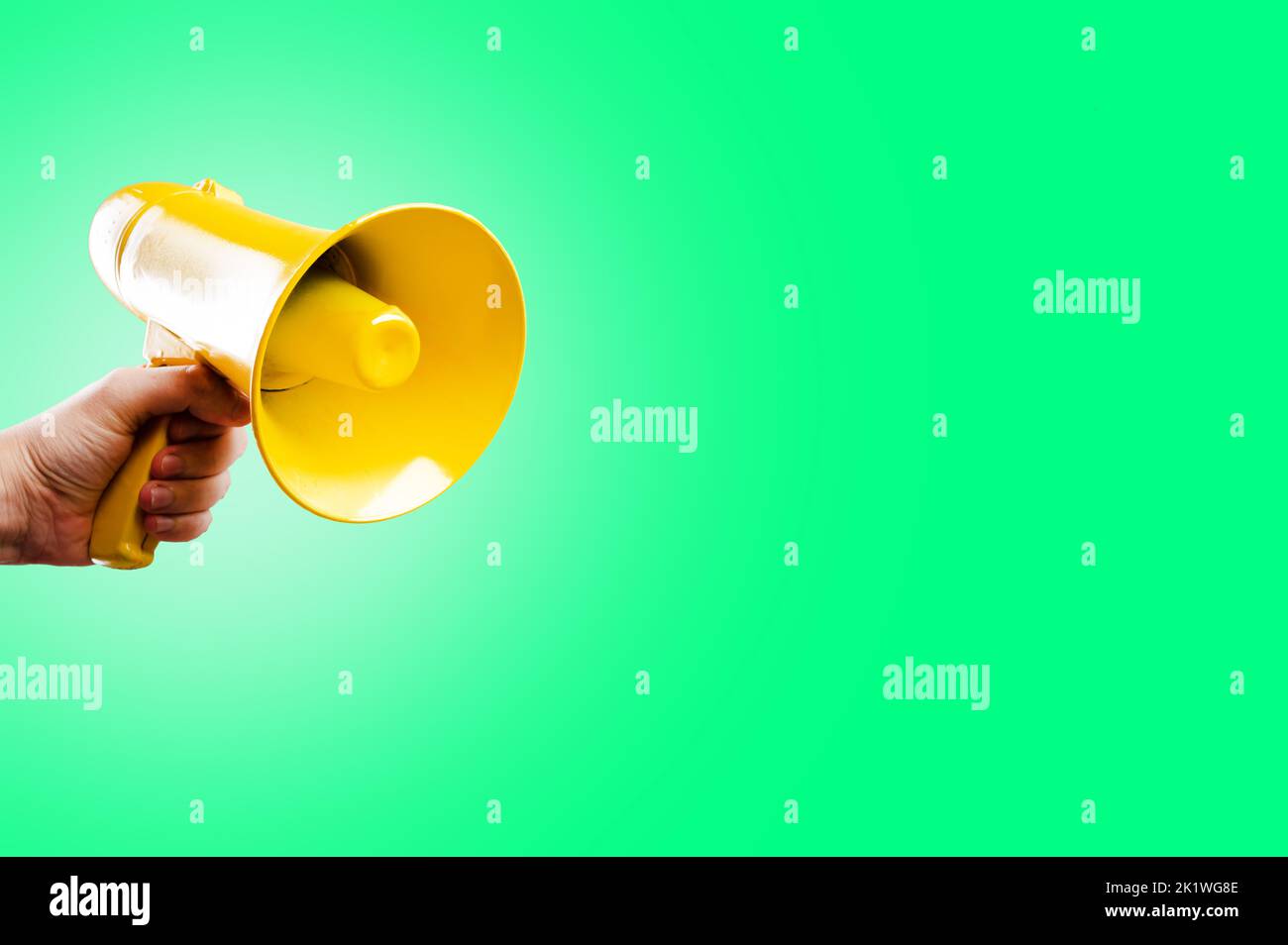 A man holds a yellow megaphone in his hand. Isolated on a green ...