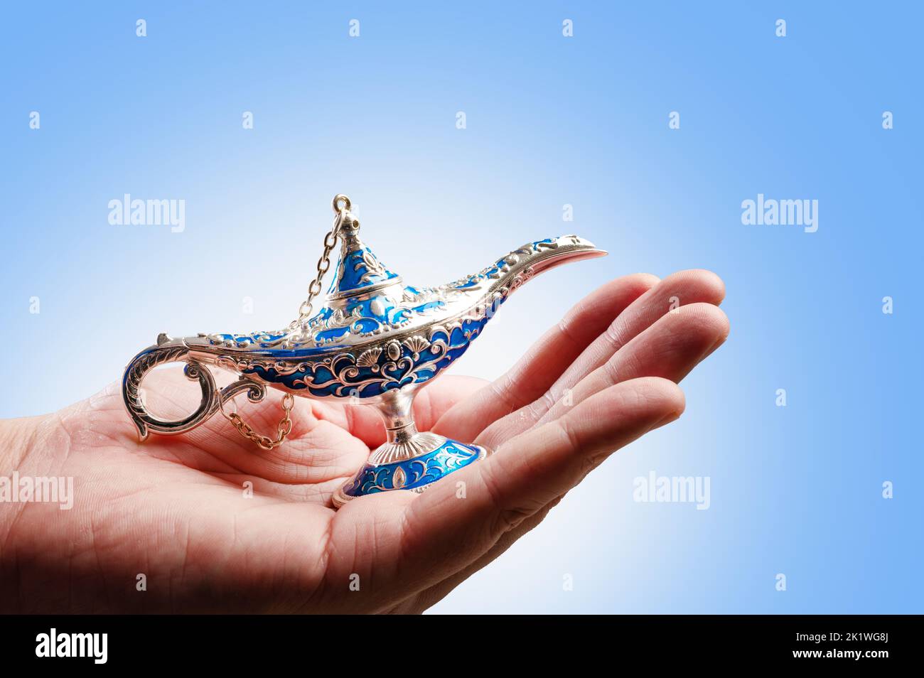 Aladdin's magical lamp in a woman's hand on a pale blue background ...