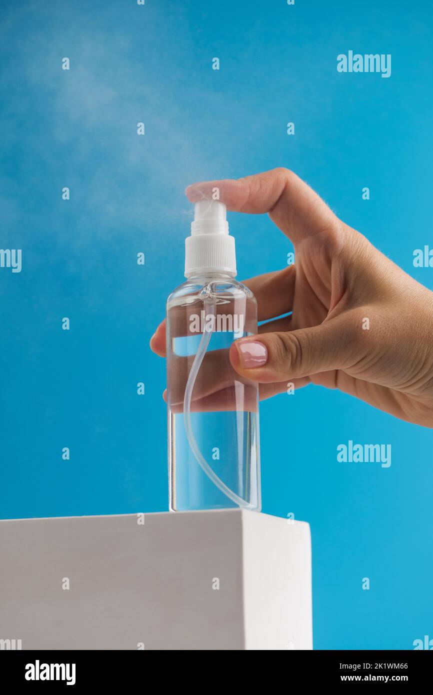 A woman's hand sprays a cosmetic product that stands on a white podium ...