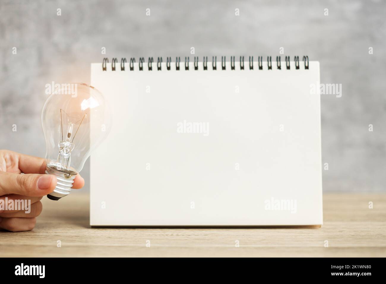 Hand holding lightbulb over blank notebook on table. New Ideas ...