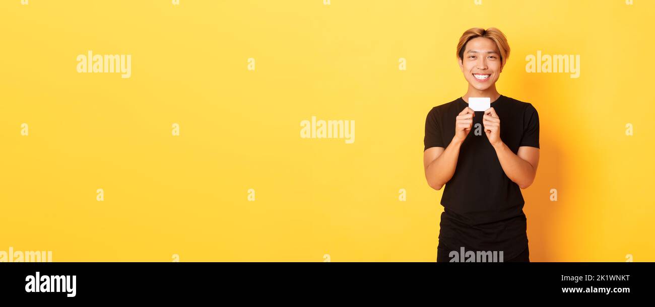 Excited happy asian guy smiling and showing credit card, standing ...