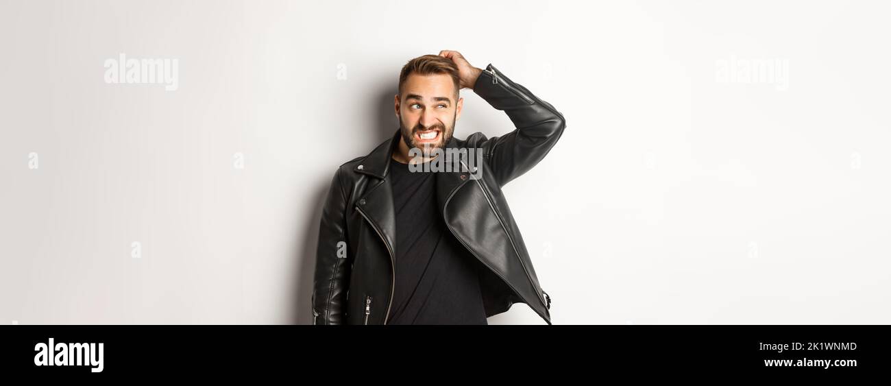 Confused macho guy in black leather jacket looking awkward and unsure ...