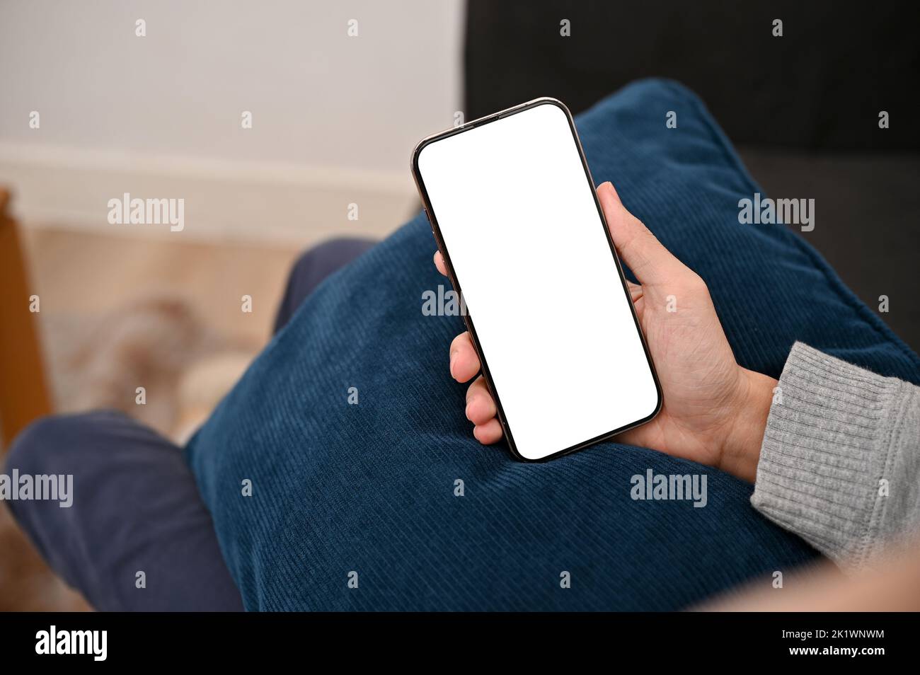 Above view, A man hand's holding a smartphone white screen mockup over his lap. Technology ...
