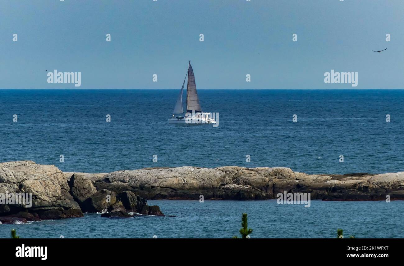 A beautiful shot of a sailing boat in the sea near the rocks in Newport ...