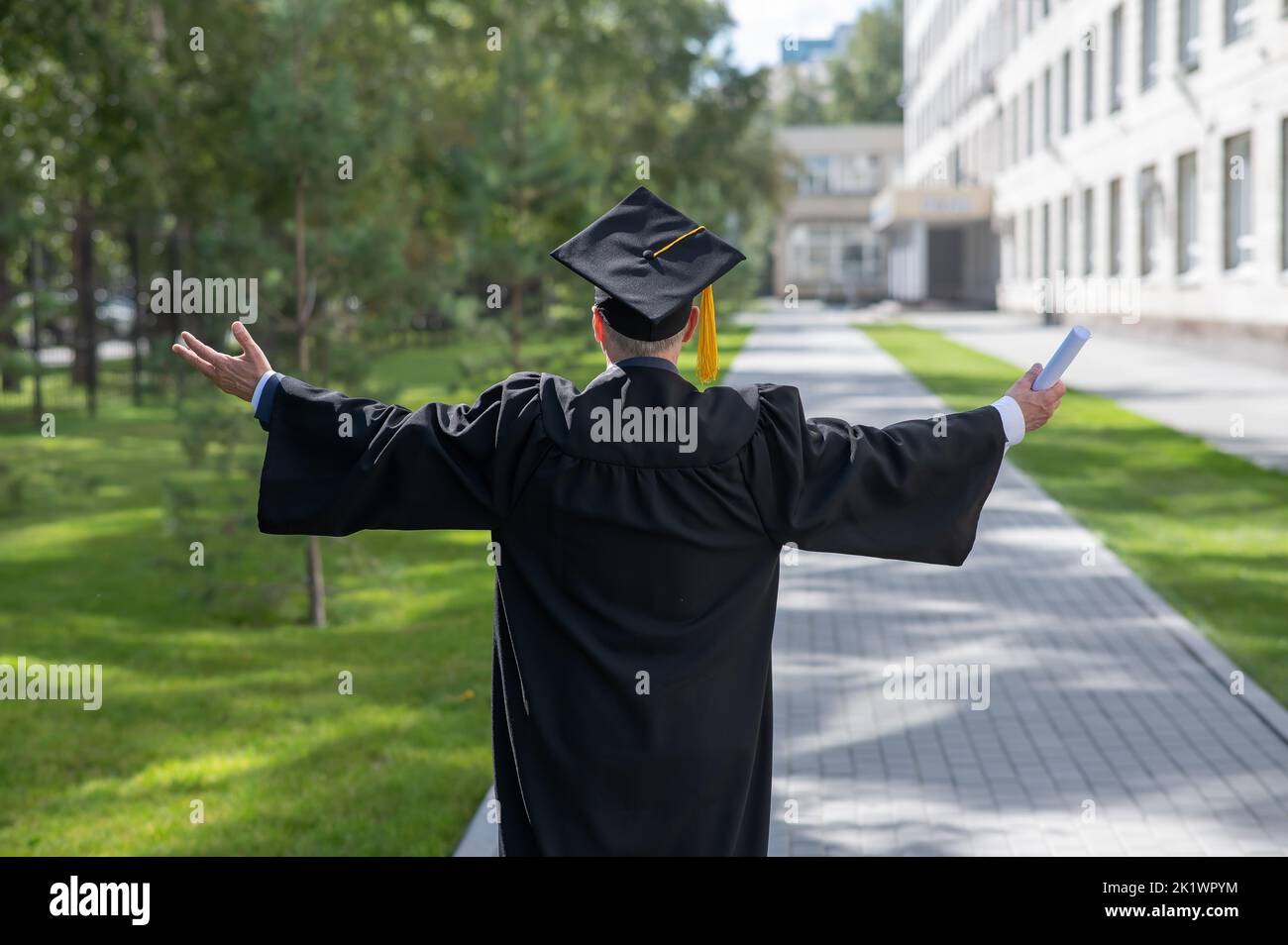 Elderly male graduate rejoices at graduation outdoors. Rear view of a ...
