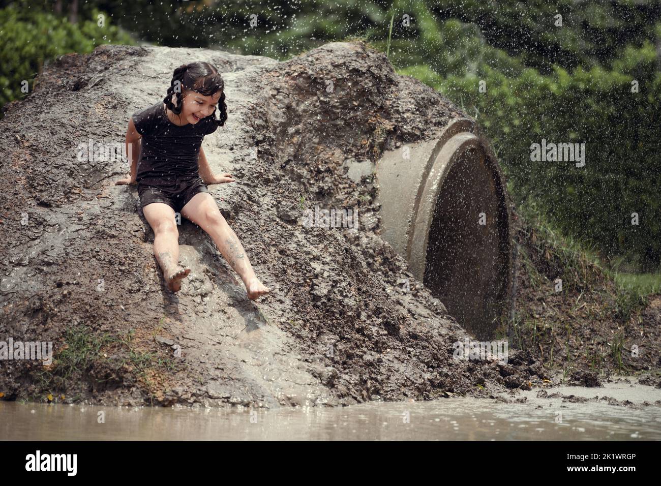 Cheerful child girl playing on heap of wet soil during raining in rainy ...