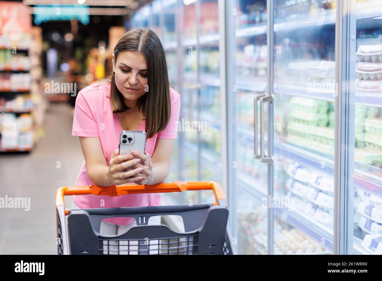 Happy caucasian woman using mobile phone in grocery shopping. Checklist ...