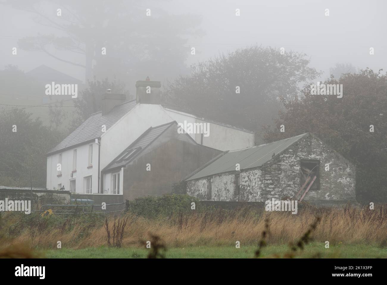 Stone crofters cottage and modern house behind. A misty day in rural ...