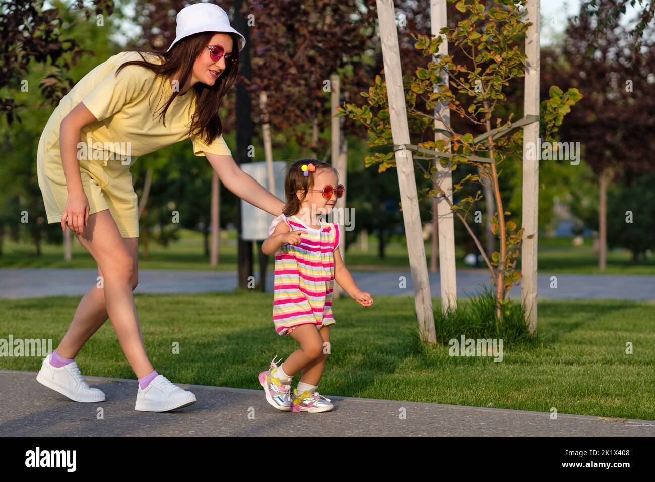 Child girl learns to take first steps in summer public park. Toddler ...
