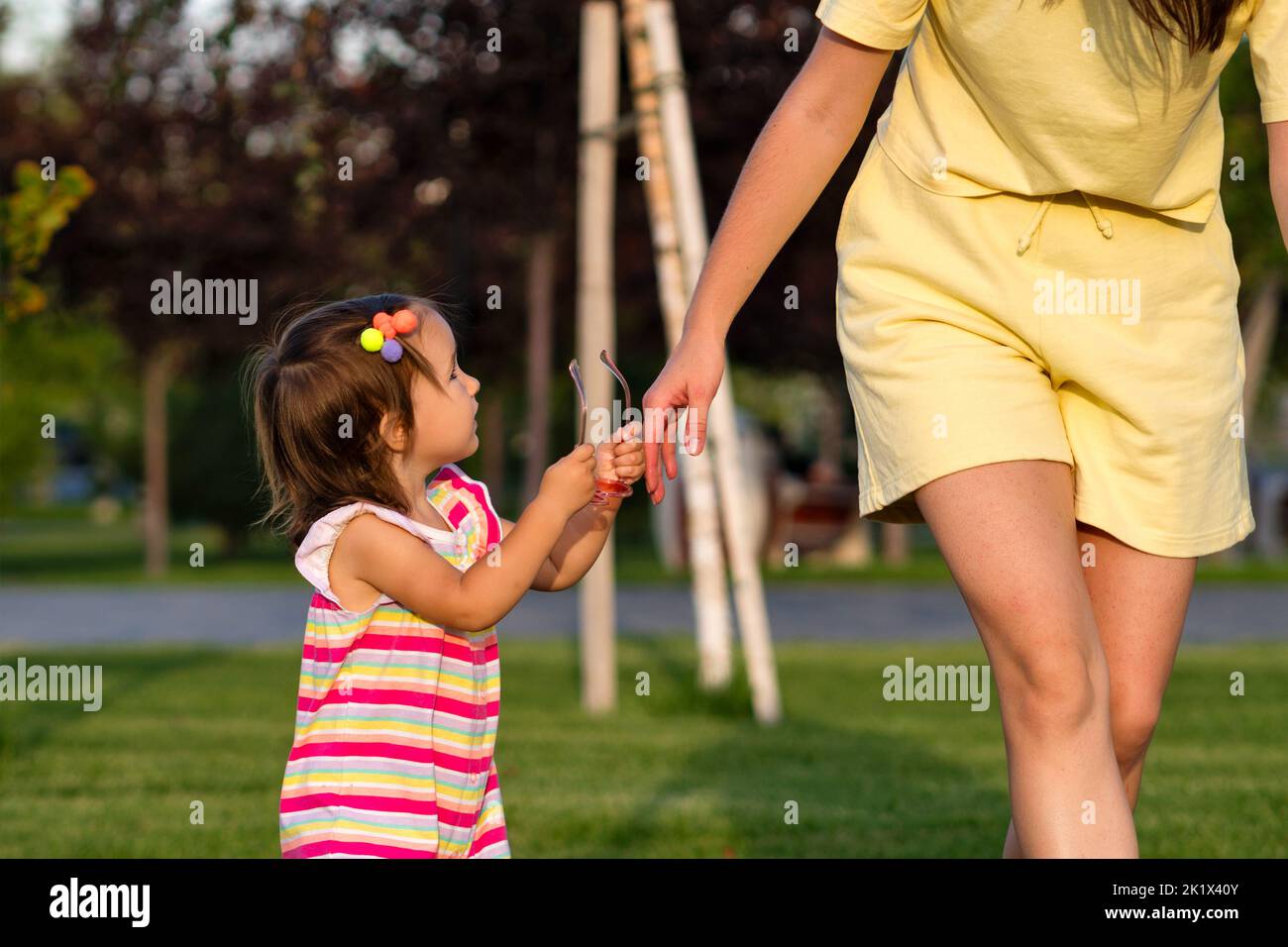 Child girl learns to take first steps in summer park. Toddler holding ...