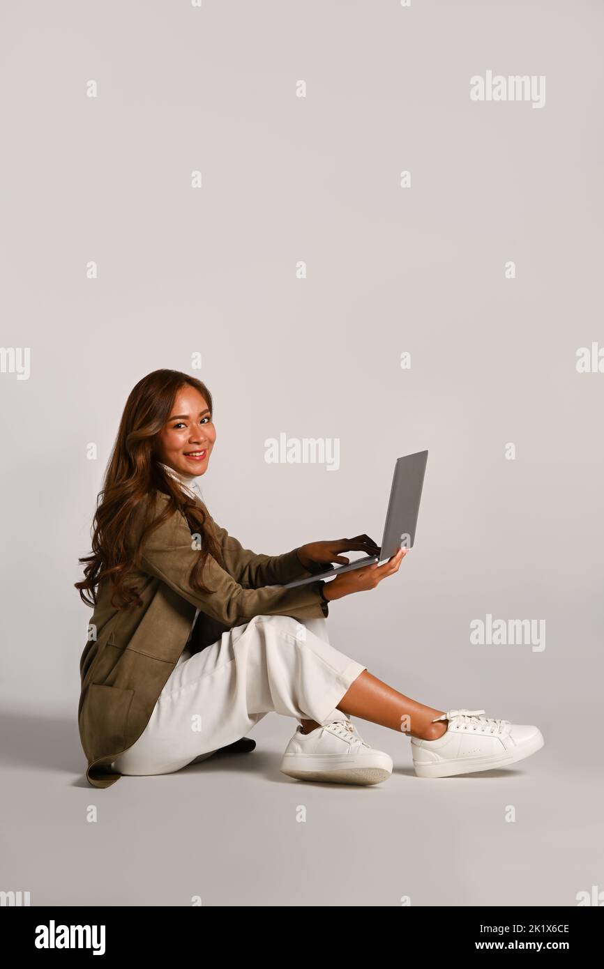 Image of attractive woman intrench coat sitting over white background and using laptop computer ...