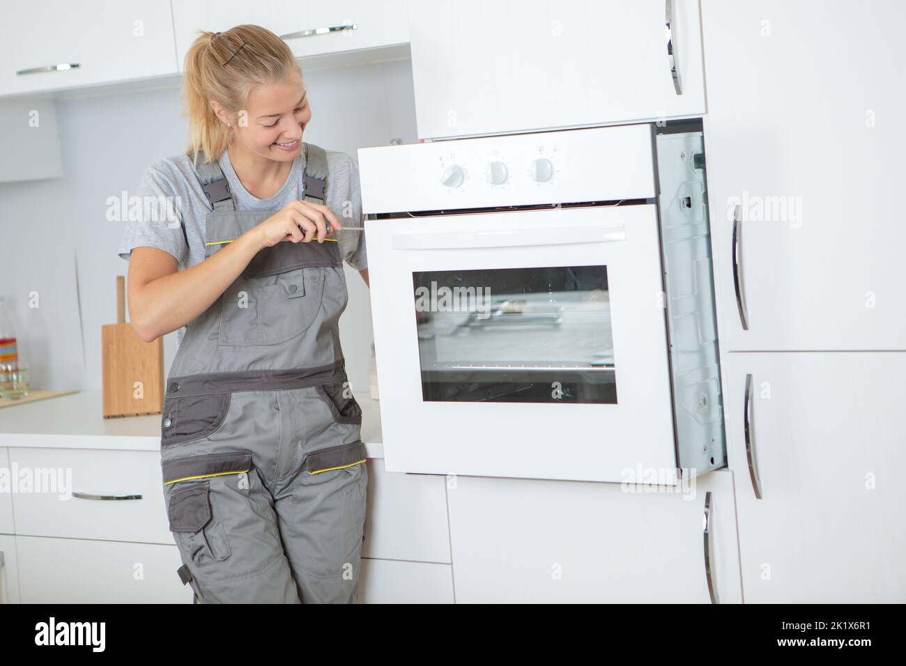 young woman looking oven using screw driver Stock Photo - Alamy