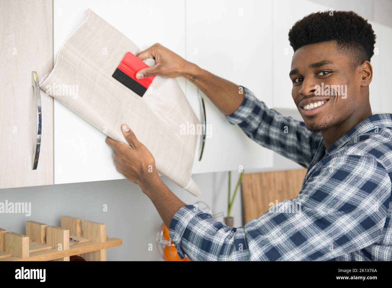 man refurbishing kitchen cupboard with adhesive veneer Stock Photo - Alamy