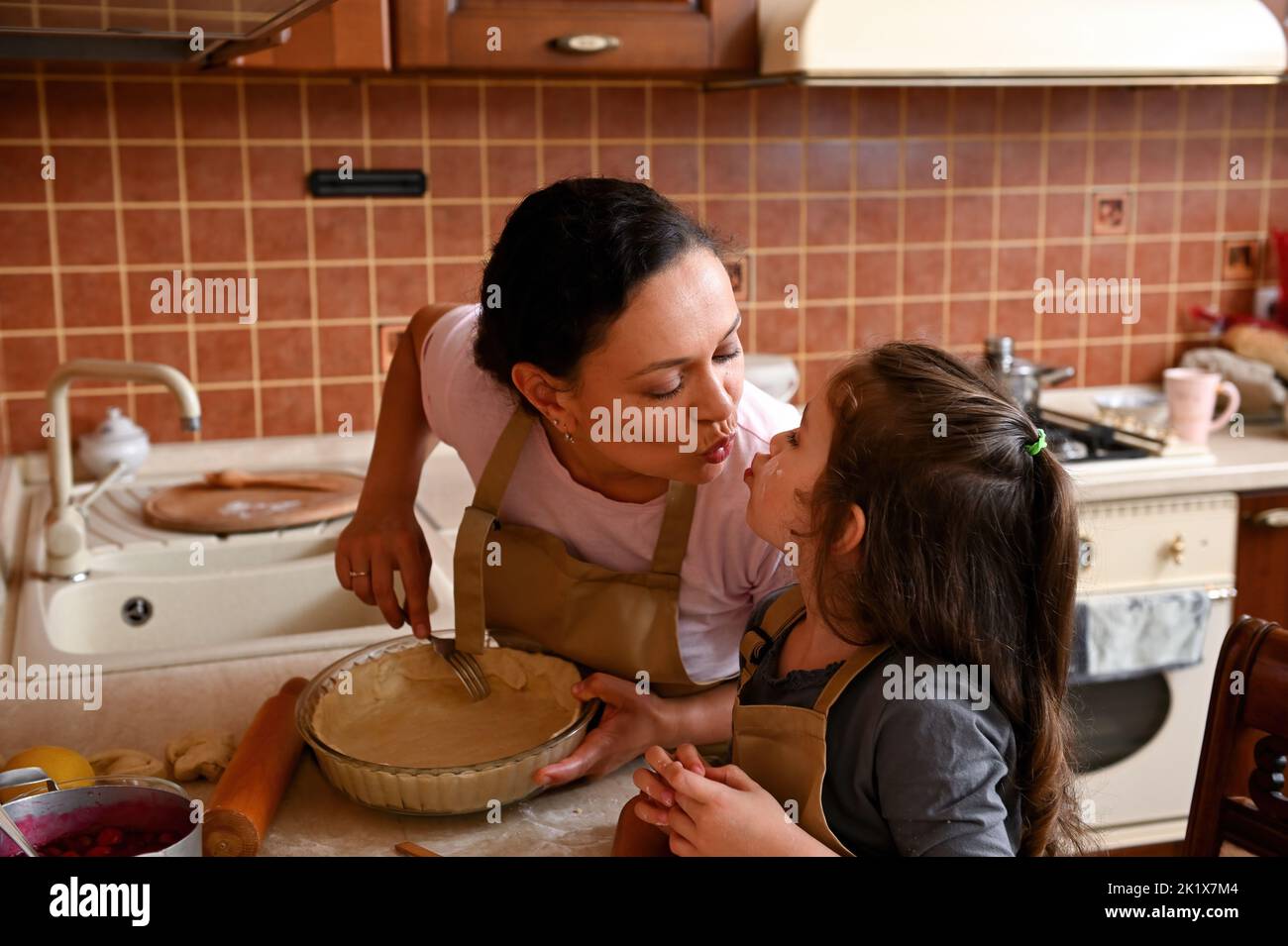 Loving mother kissing her cute baby, lovely daughter while cooking ...