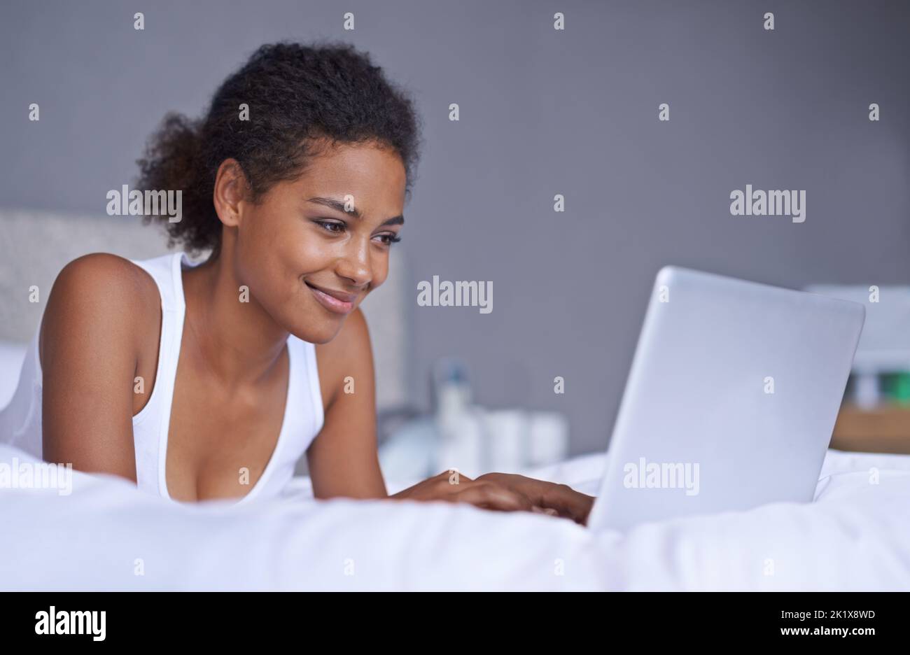 Catching up with an old friend. a young woman lying on a bed using a ...