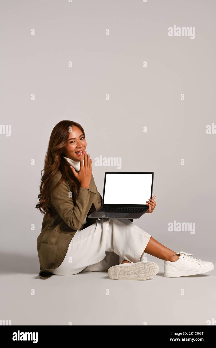 Image of attractive woman intrench coat sitting over white background and using laptop computer ...