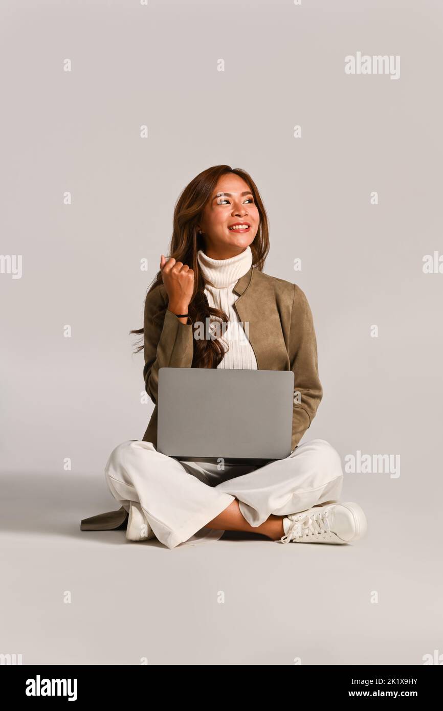Image of attractive woman intrench coat sitting over white background and using laptop computer ...