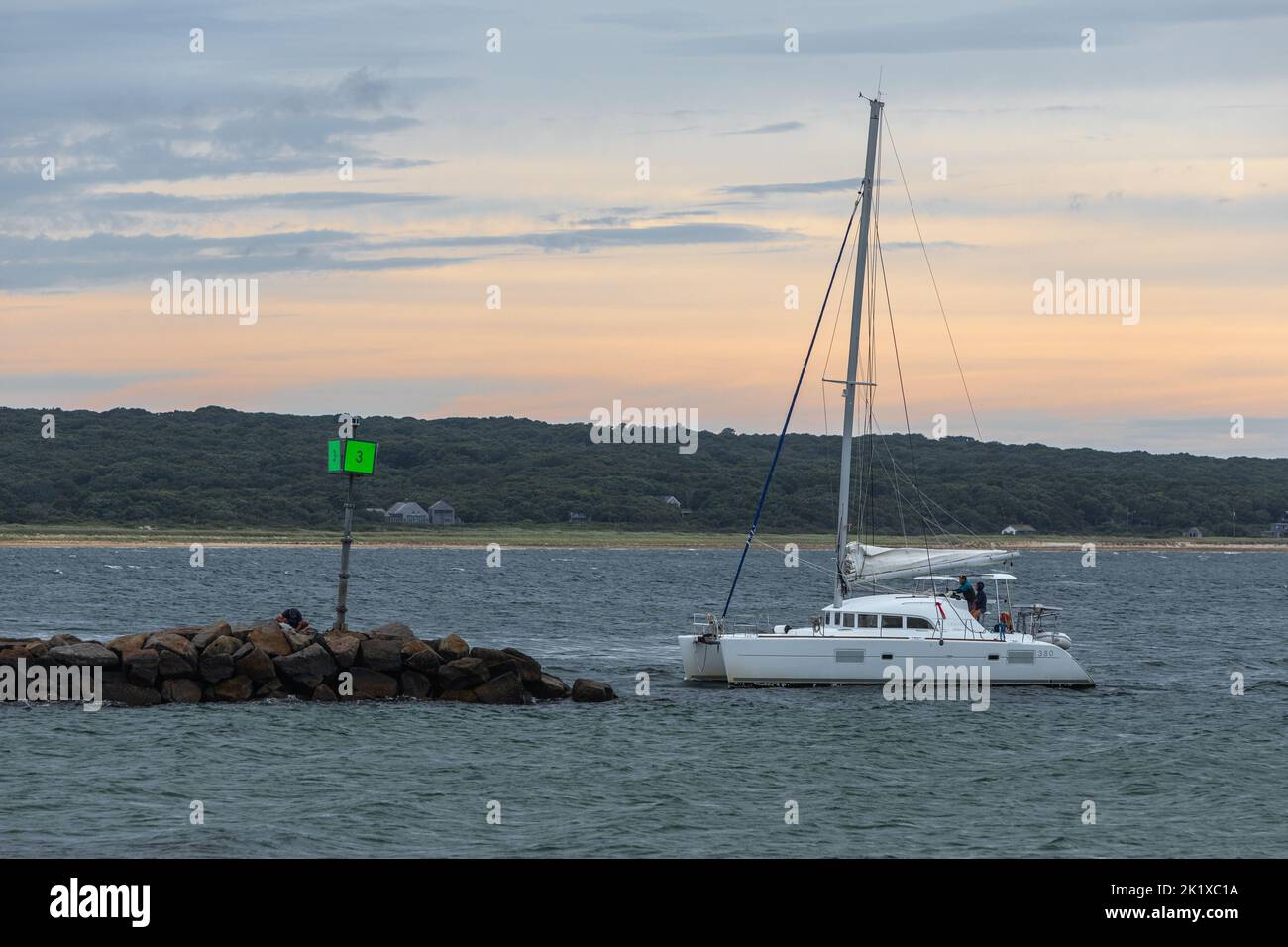 A catamaran sailboat entering a harbor on Marthas vineyard at sunset ...