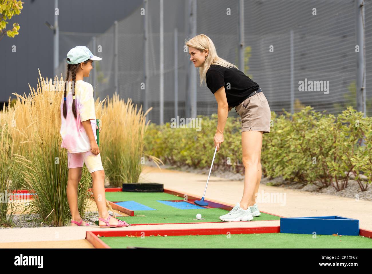 Mother playing with her cute daughter mini golf at outdoor playground ...