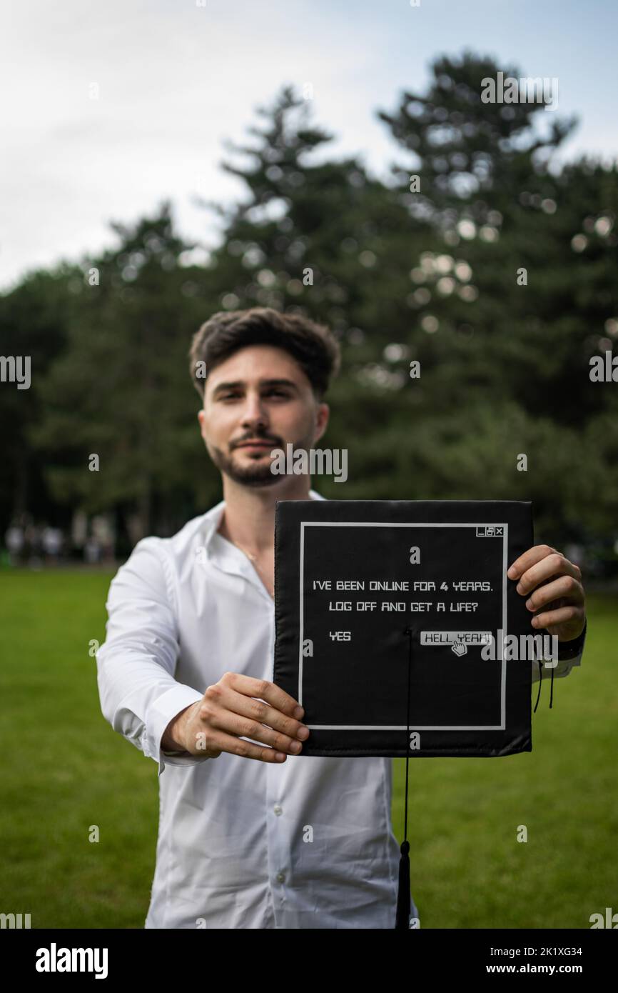 A vertical of a Caucasian young guy smiling and holding his cap on his ...