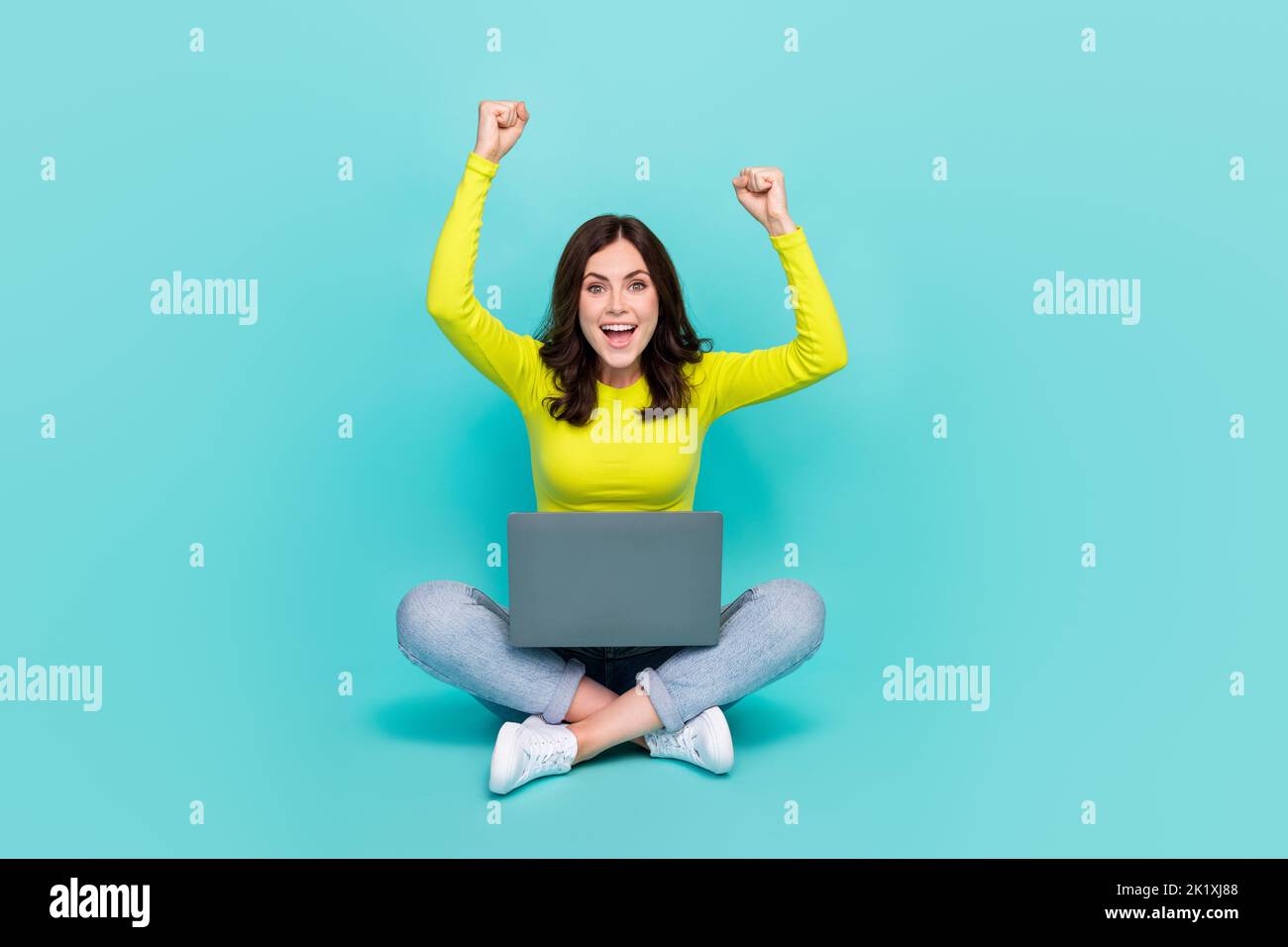 Full size portrait of overjoyed positive girl sit floor raise hands use netbook isolated on teal ...