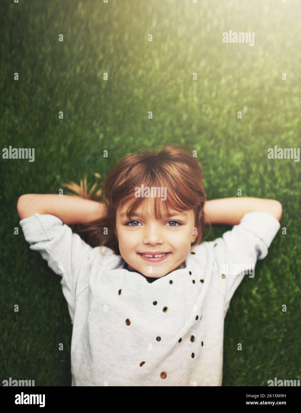 Born to be happy. a cute little girl smiling while lying down on grass ...