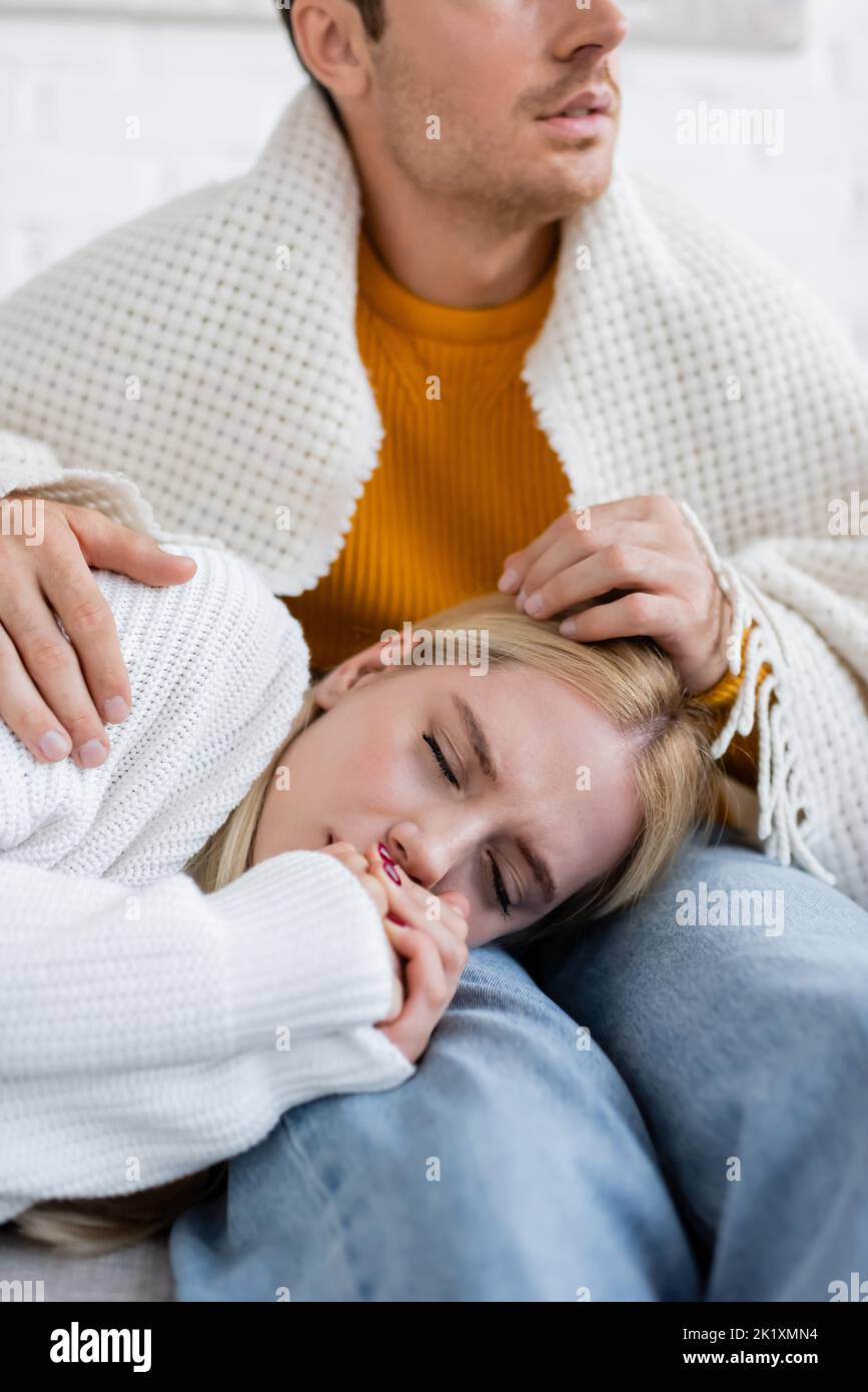 young woman covered in blanket sleeping on legs of boyfriend in jeans ...