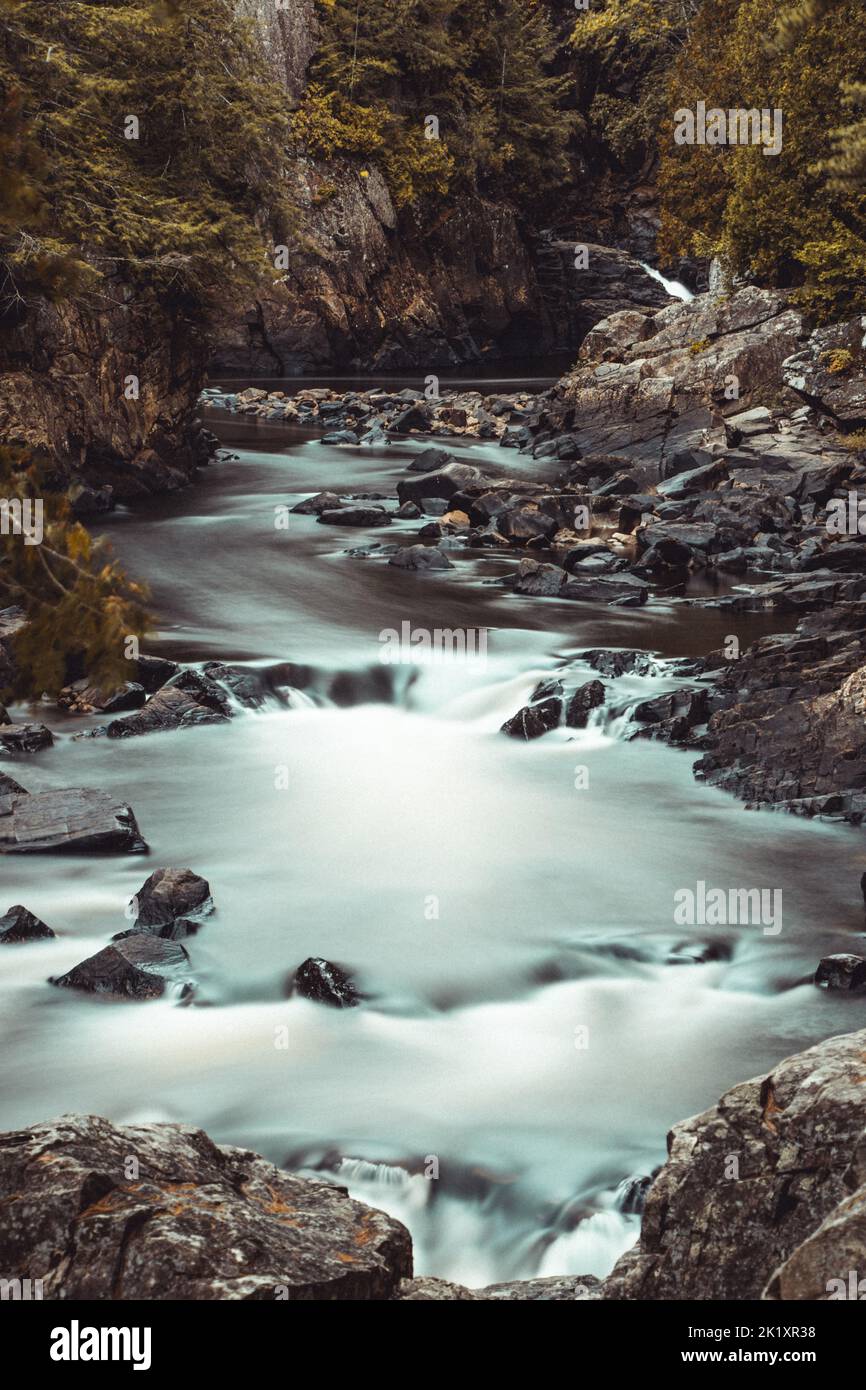 A vertical shot of the river water flowing on stones with smooth effect ...