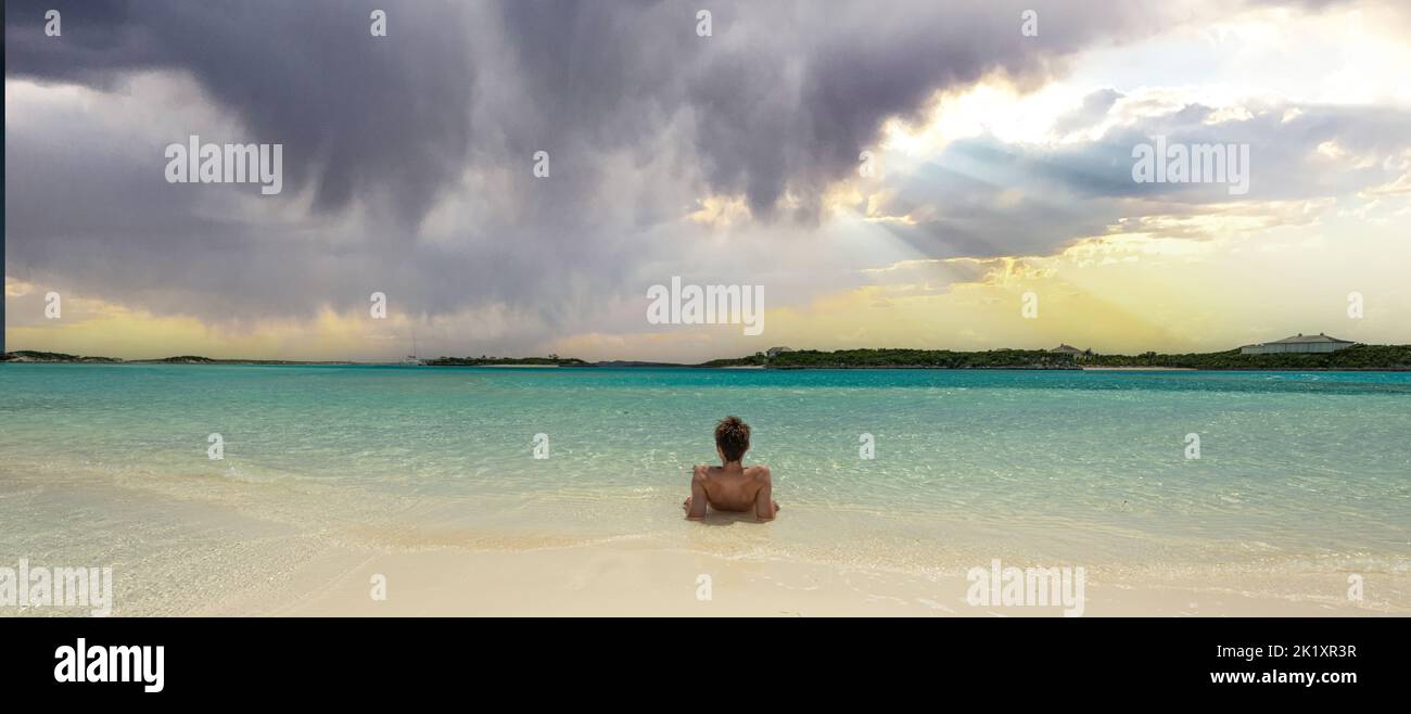 A back view of a female relaxing on a calm seashore with clear water ...