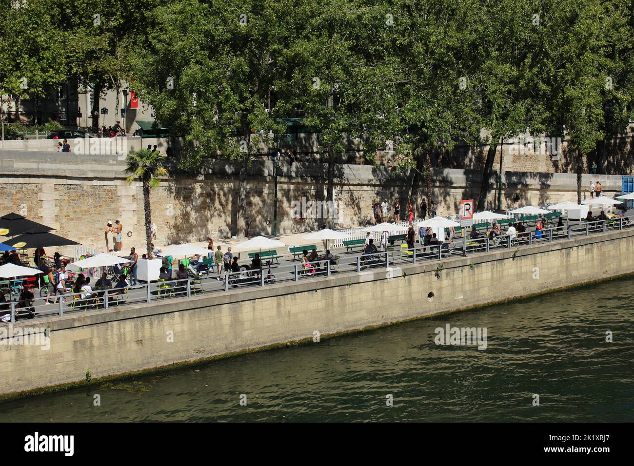 People relax beside the River Seine on a summer afternoon underneath ...