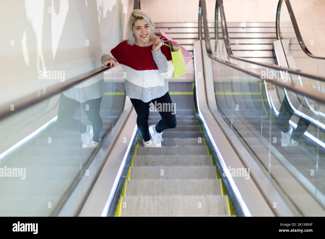 High-angle view of cheerful pretty young woman holding on escalator ...
