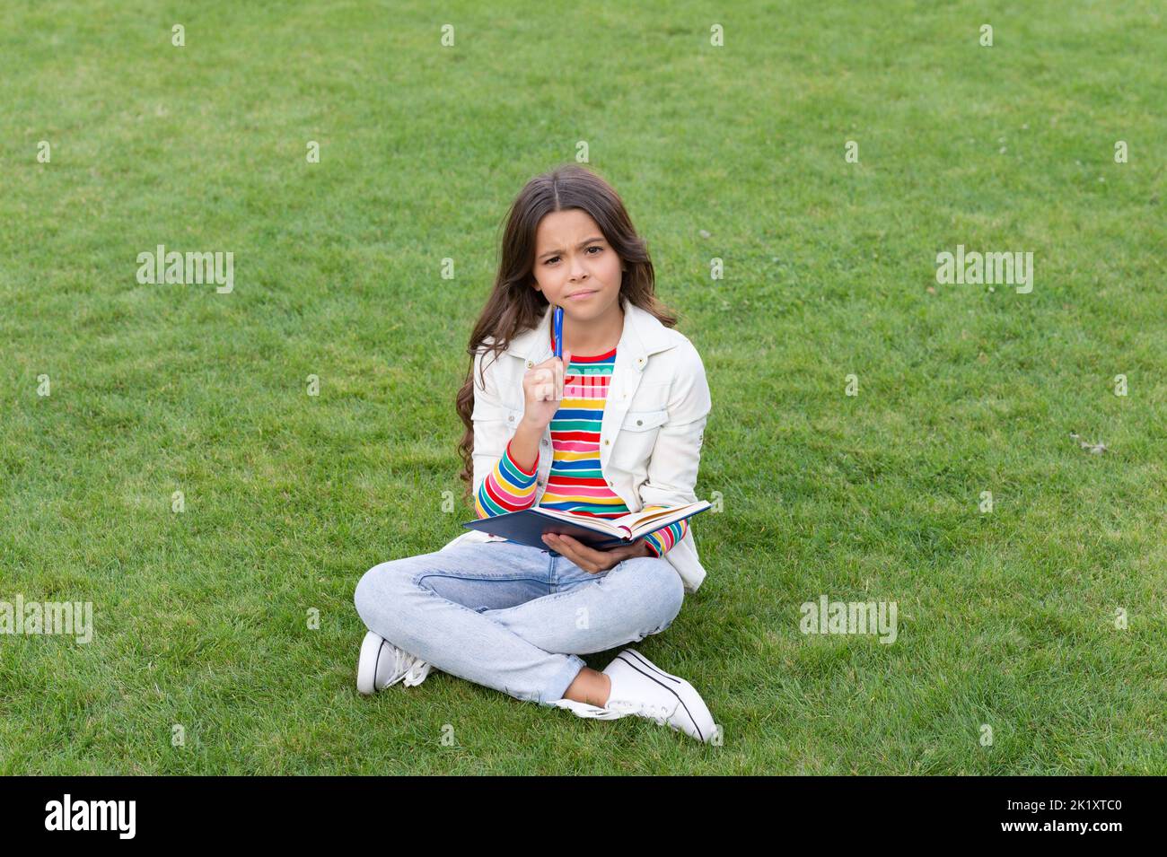 thinking teen girl making notes in notebook sitting on grass. taking ...