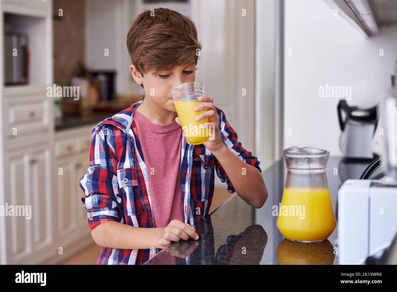 Helping himself to some juice. A young boy drinking a glass of orange ...