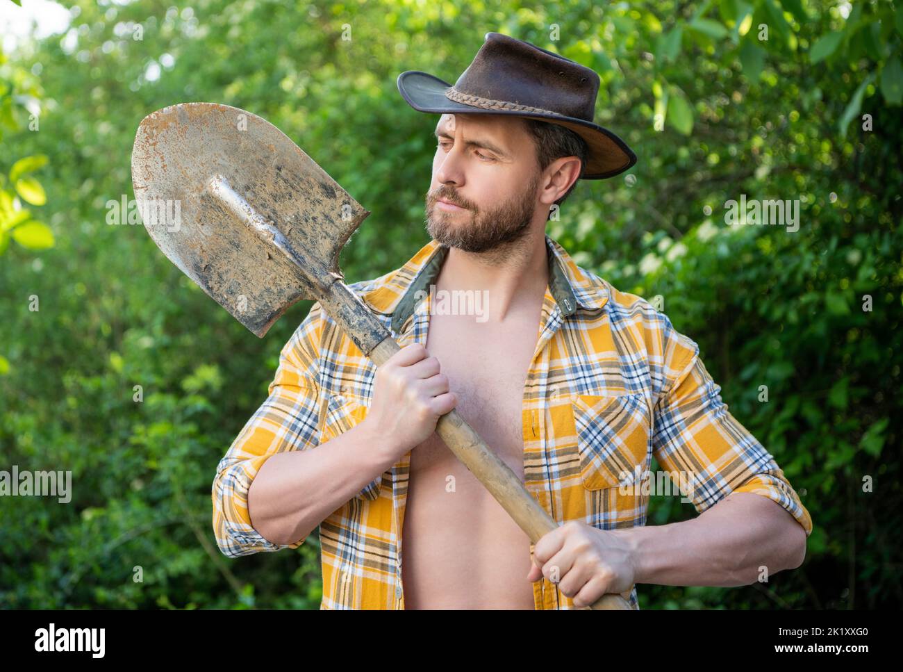 Serious guy holding garden spade. Unshaven guy wearing cowboy hat and ...